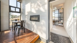 Interior moderno com deck de madeira, área de jantar com mesa e cadeiras, e vista para o exterior através de grandes janelas.