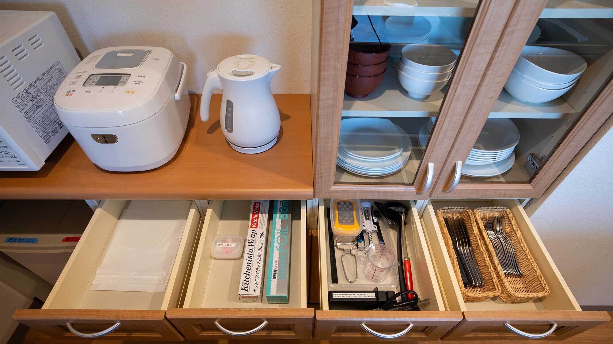 Uma área de cozinha com um cozedor de arroz, uma cafeteira e um armário com utensílios e louças.