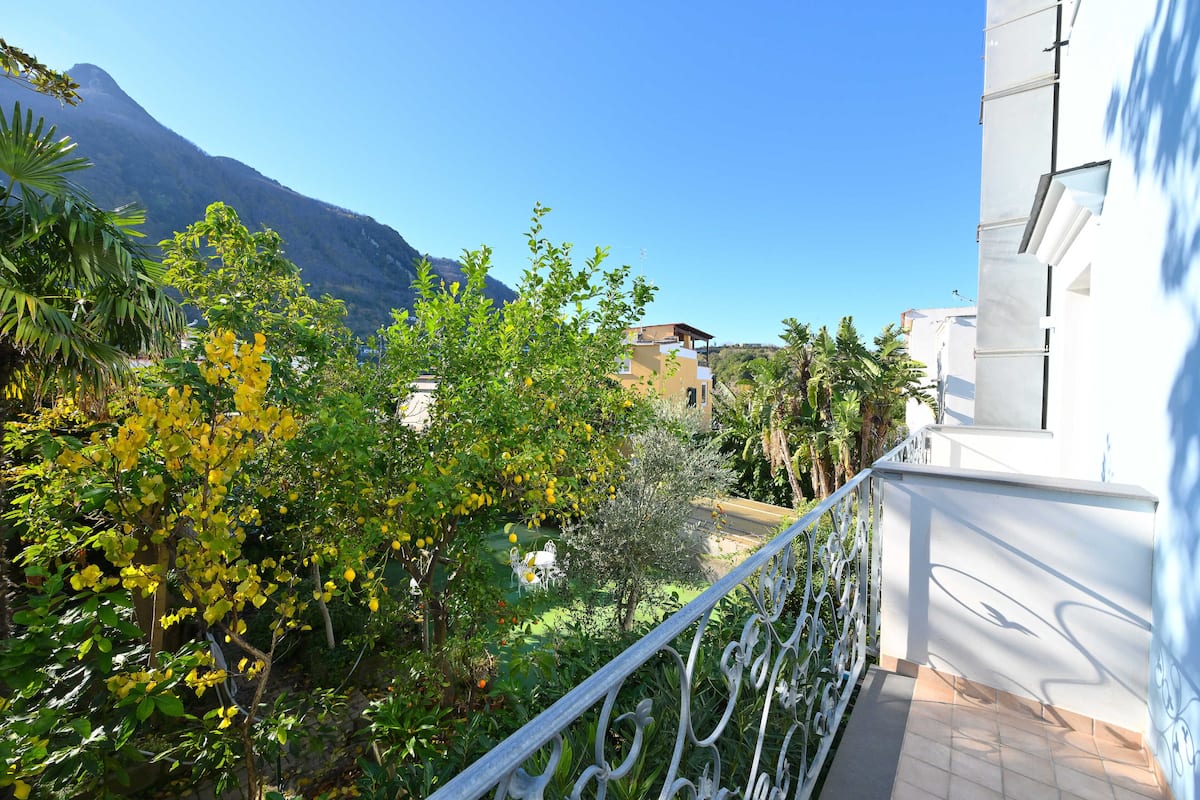Varanda com vista para uma montanha, vegetação e um edifício branco.