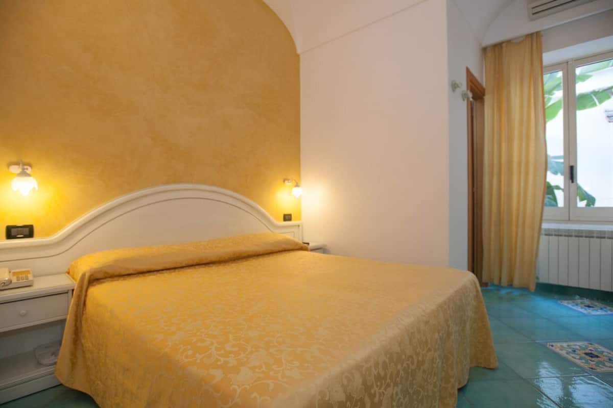 Quarto de hotel com cama, abajures, mesa de cabeceira e janela com cortinas.