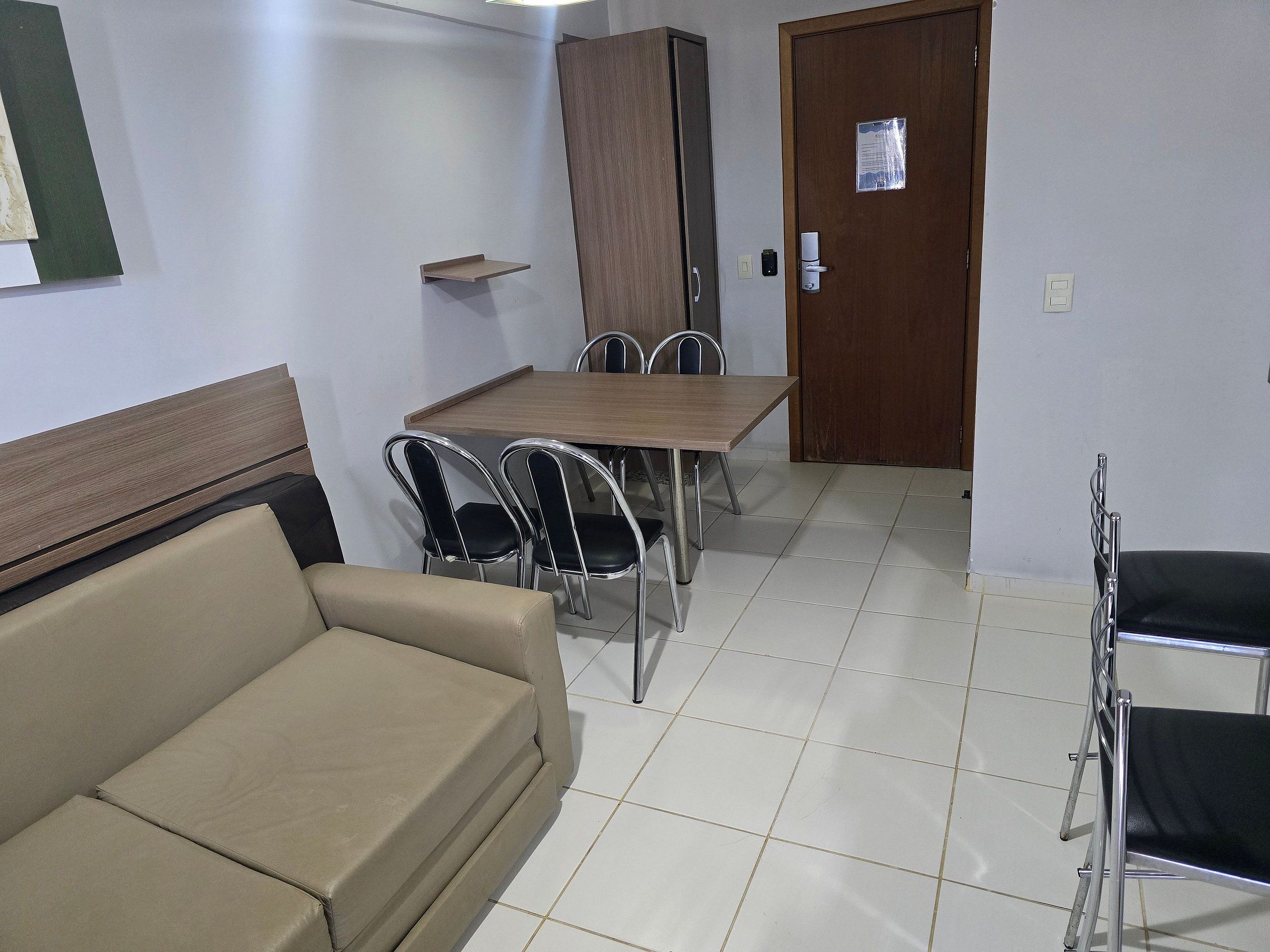 Quarto pequeno e limpo, com uma mesa de jantar de madeira, quatro cadeiras, um sofá e um armário.