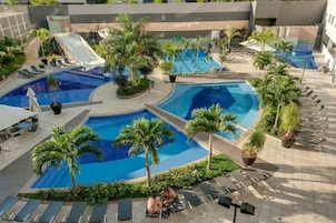 Uma área de piscina no terraço com várias piscinas, palmeiras e espreguiçadeiras.