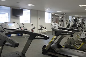 Uma academia com esteiras, aparelhos de musculação e uma TV na parede.