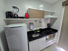 Uma cozinha compacta equipada com geladeira, cafeteira, chaleira e micro-ondas.