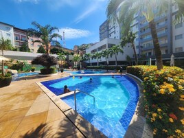 Uma área de piscina com várias piscinas, palmeiras e um edifício ao fundo.