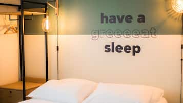 Uma cama com roupa de cama branca em um quarto com luminária na parede e uma parede com texto.