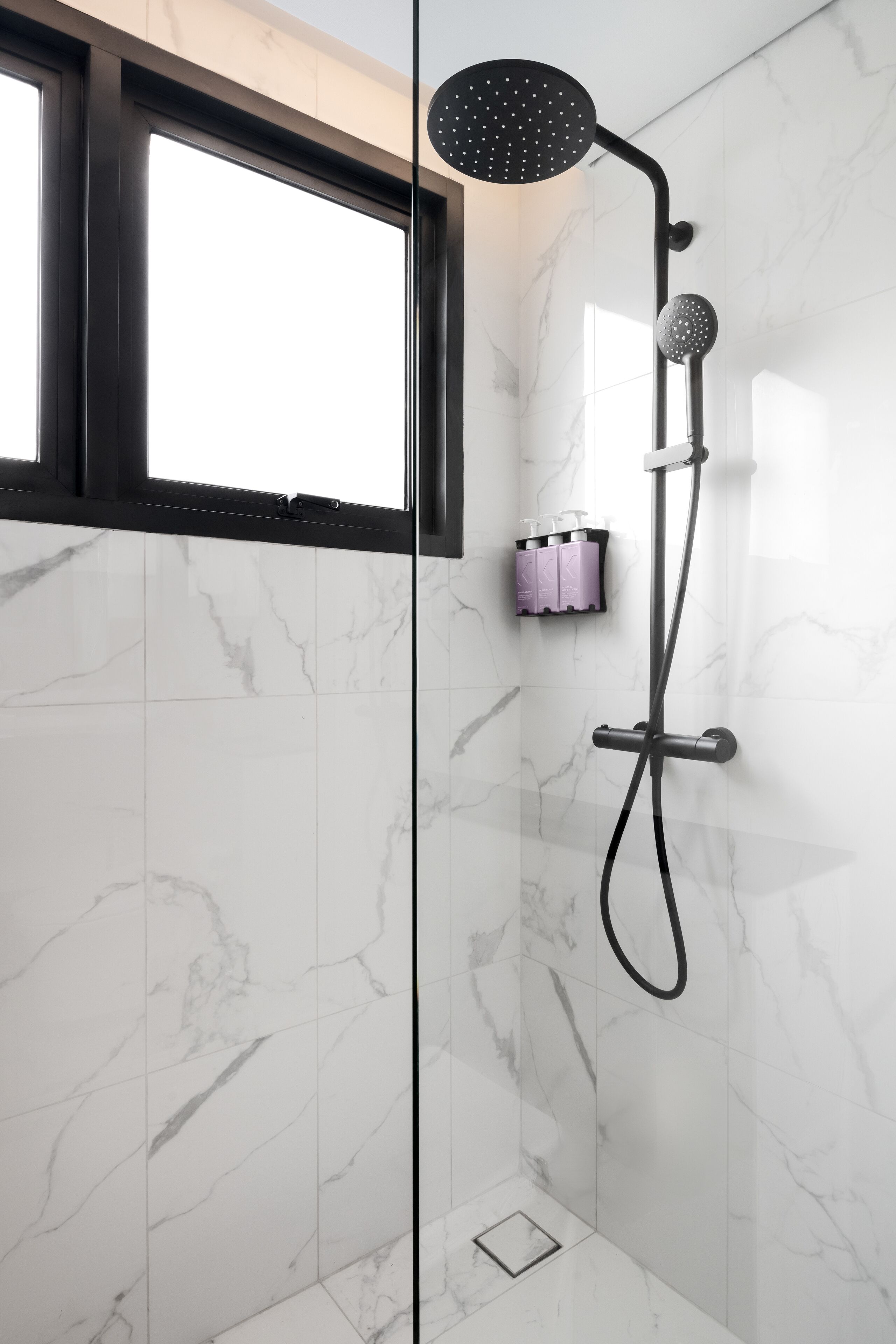 Chuveiro moderno com chuveiro manual, painel de controle fixado na parede e divisória de vidro.