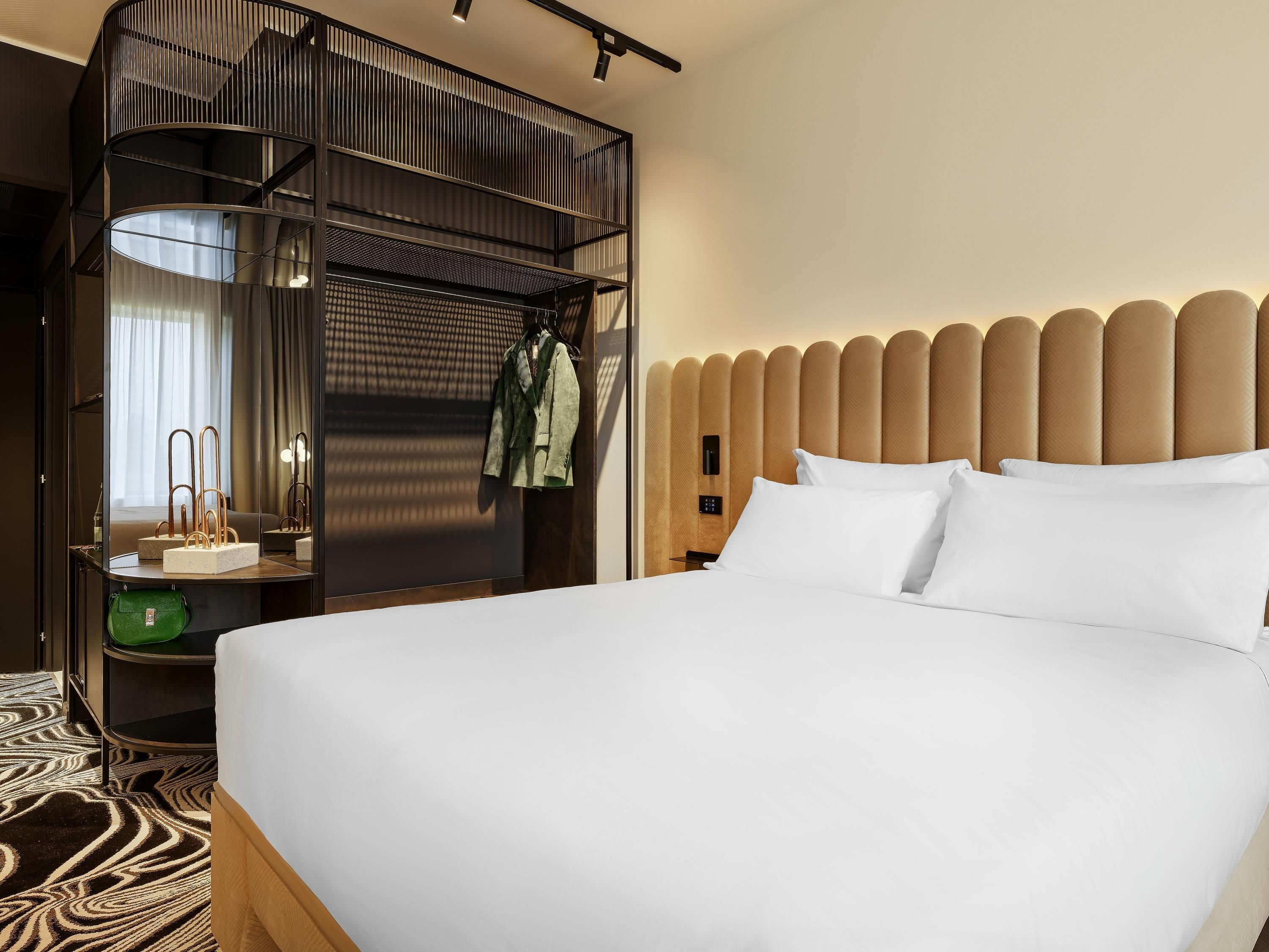 Quarto de hotel com cama, espelho, guarda-roupa e mesa de cabeceira.