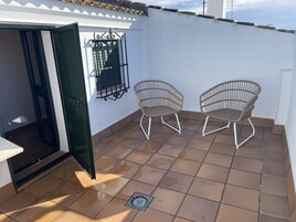 Um pequeno pátio externo com duas cadeiras de vime, um portão de metal e piso de azulejos.