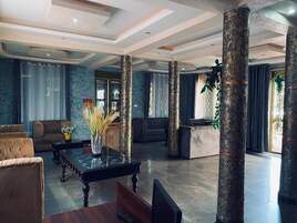 Um hall amplo com pé direito alto, colunas decorativas e diversos arranjos de assentos, incluindo sofás e poltronas.