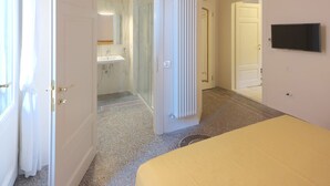 Quarto de hotel com cama, televisão, banheiro com pia e espelho, e radiador.