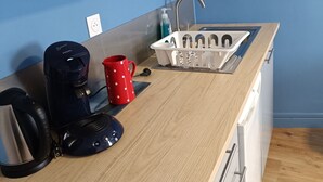 Uma cozinha compacta com cafeteira, caneca vermelha, pia com dispensador de sabonete e micro-ondas sobre o balcão.