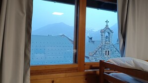 Um quarto com uma cama beliche de madeira, uma janela com cortinas e vista para uma igreja com torre do sino.