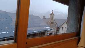 Visão pela janela de um edifício com uma igreja de pedra e telhados cobertos de neve.
