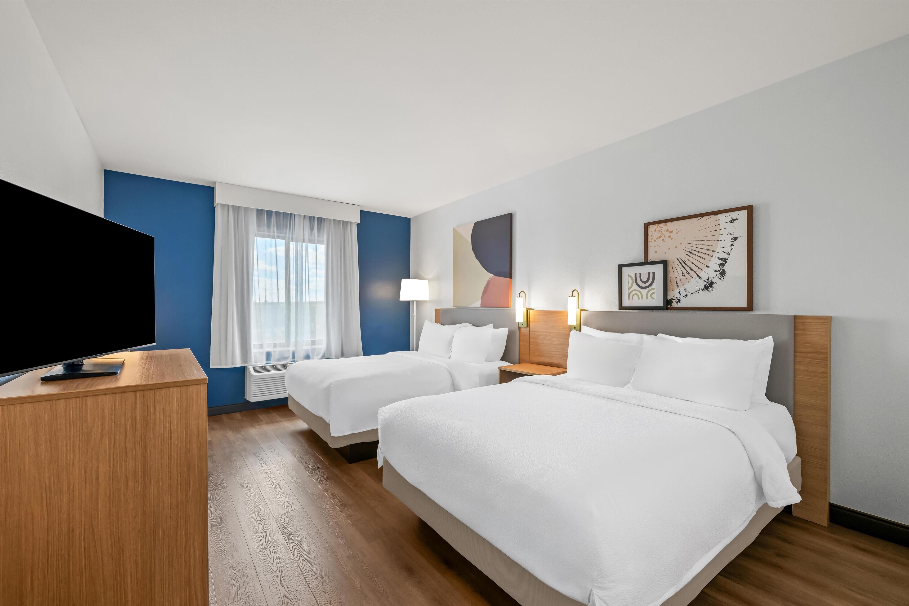 Quarto de hotel com duas camas, televisão e obras de arte nas paredes.