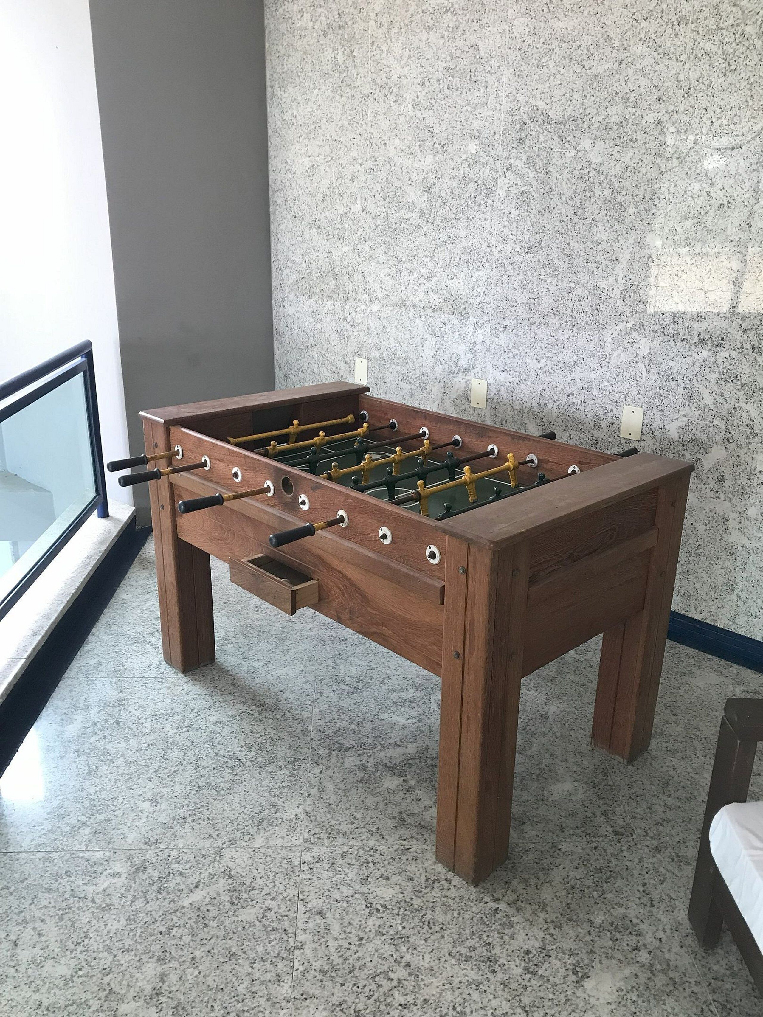 Uma mesa de futebol de madeira numa sala com chão salpicado e parede cinza.