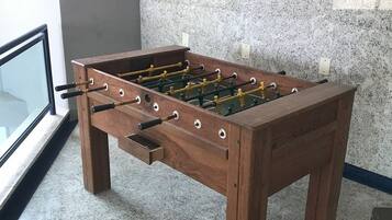 Uma mesa de futebol de madeira numa sala com chão salpicado e parede cinza.