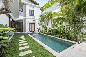 Uma casa moderna com piscina, cercada por vegetação exuberante e um gramado bem cuidado.