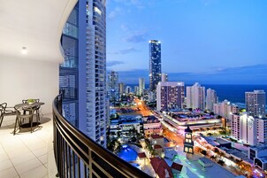 Hotel alto com varanda, apresentando área de refeições, piscina e vista para a cidade e oceano.