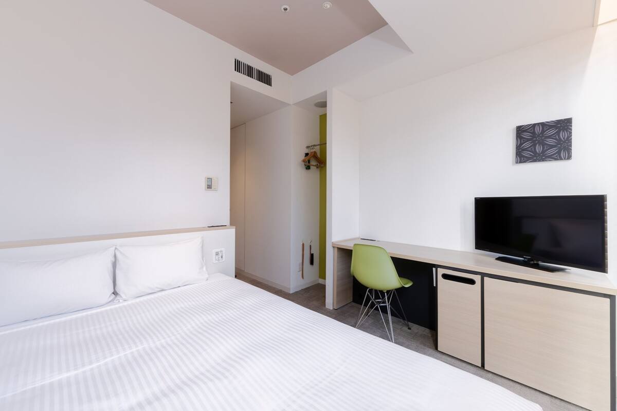 Quarto de hotel moderno com uma cama grande, uma escrivaninha com cadeira, televisão de tela plana e uma kitchenette.