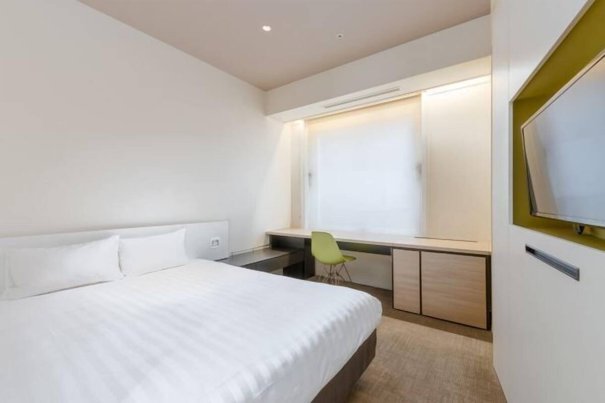 Quarto de hotel moderno com uma cama grande, uma mesa de trabalho, uma cadeira e uma televisão.
