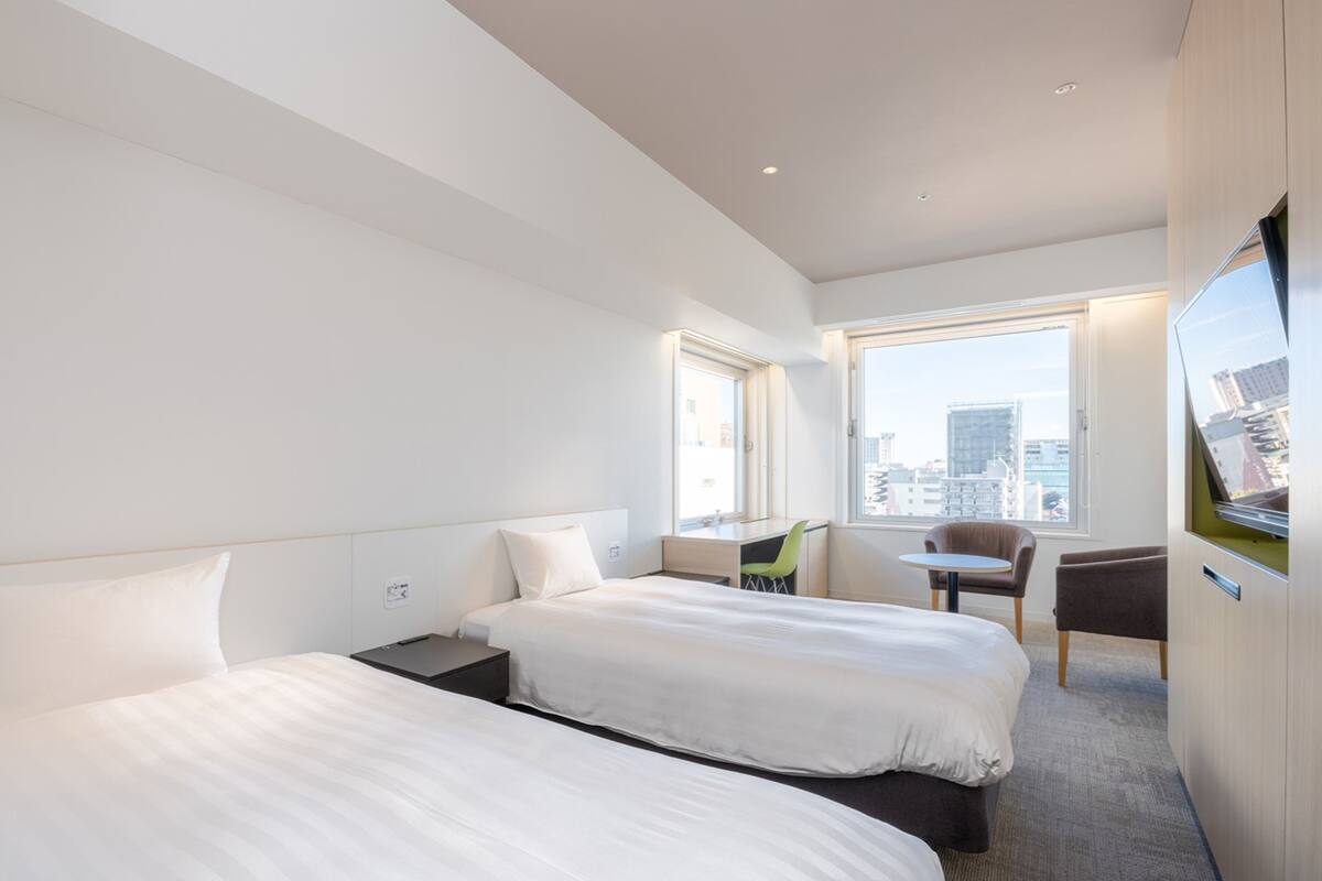 Quarto de hotel moderno com duas camas, uma escrivaninha, uma cadeira e uma televisão.