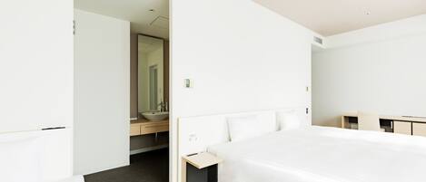 Quarto de hotel moderno com uma cama grande, mesa de cabeceira, escrivaninha e banheiro com pia e espelho.