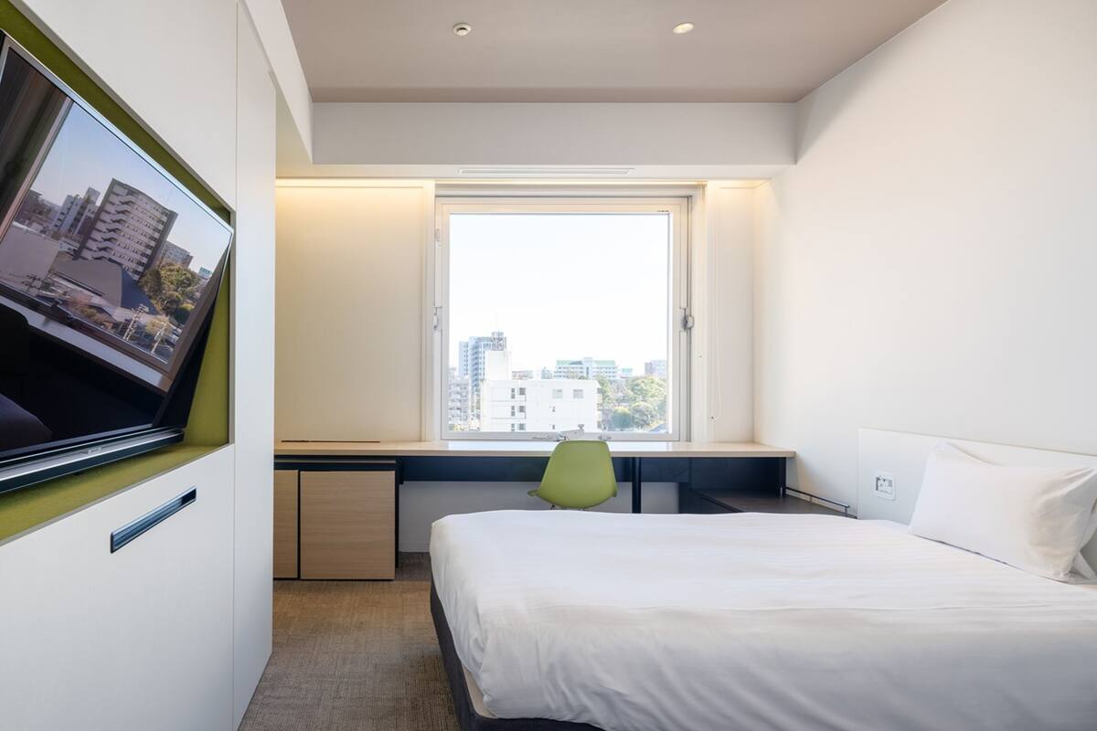 Quarto de hotel moderno com uma cama grande, uma escrivaninha e uma TV fixada na parede.