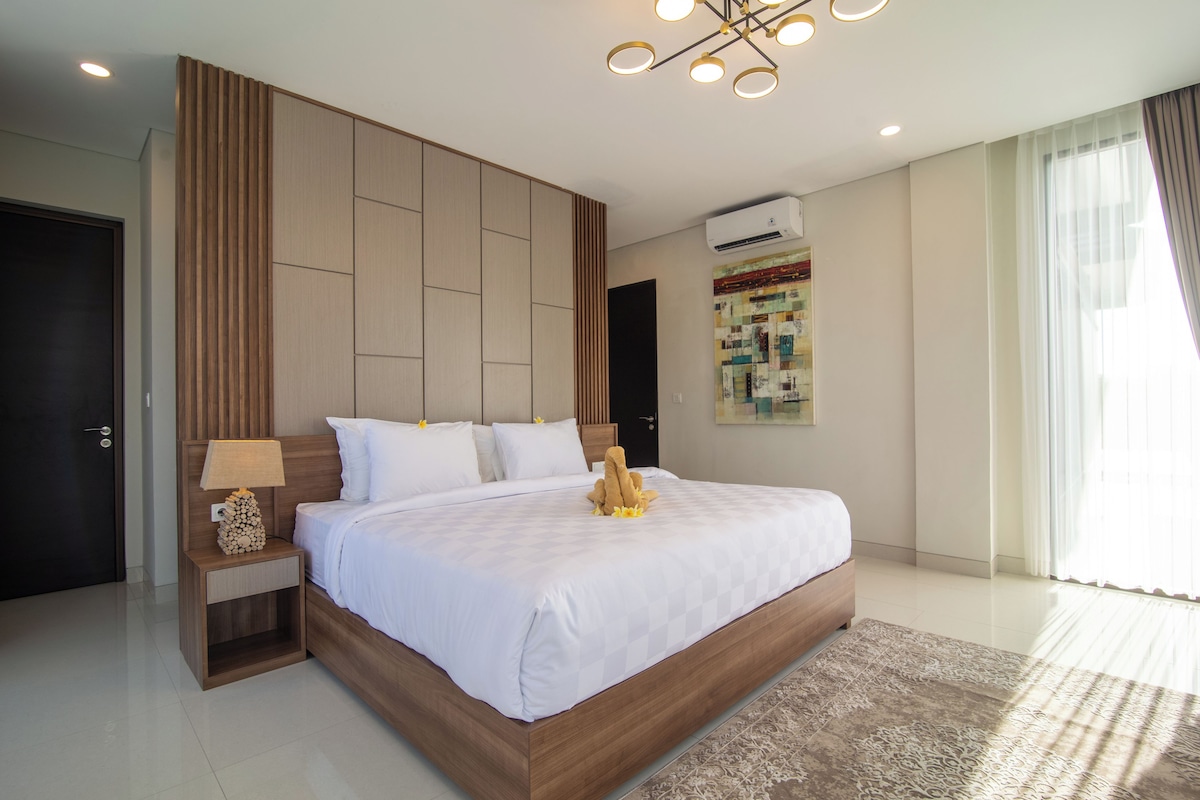 Quarto moderno com uma cama grande, lambris de madeira, mesa de cabeceira com abajur e luminária no teto.
