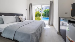Quarto de hotel com cama, televisão, mini-geladeira e vista para a piscina.