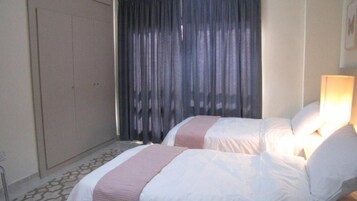 Quarto de hotel com duas camas, um guarda-roupa e uma cortina.