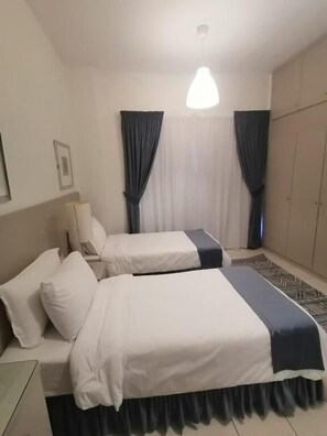 Quarto de hotel com duas camas, uma escrivaninha, uma luminária e um guarda-roupa.