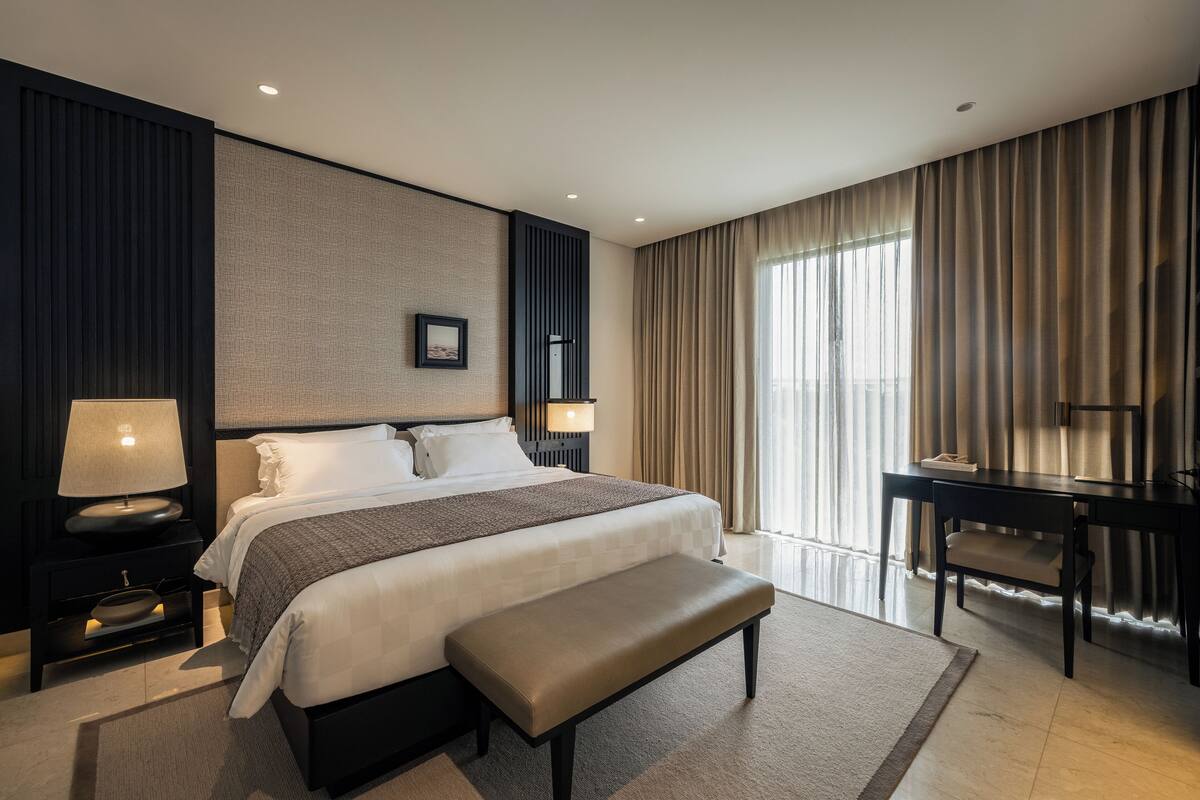 Quarto de hotel moderno com uma cama grande, uma mesa e um banco.