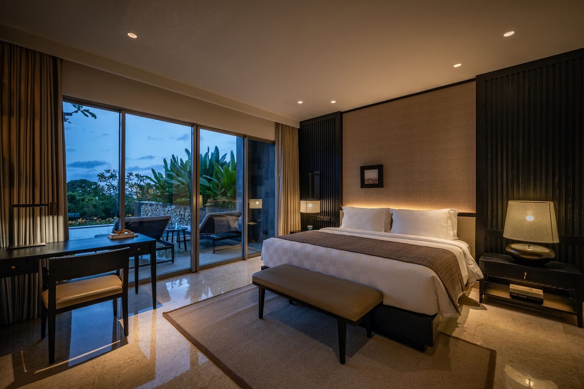 Quarto de hotel moderno com uma cama grande, uma mesa de trabalho e vista para o exterior.