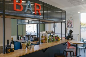 Uma área de bar com balcão exibindo diversos frascos e copos, uma máquina de café e assentos.