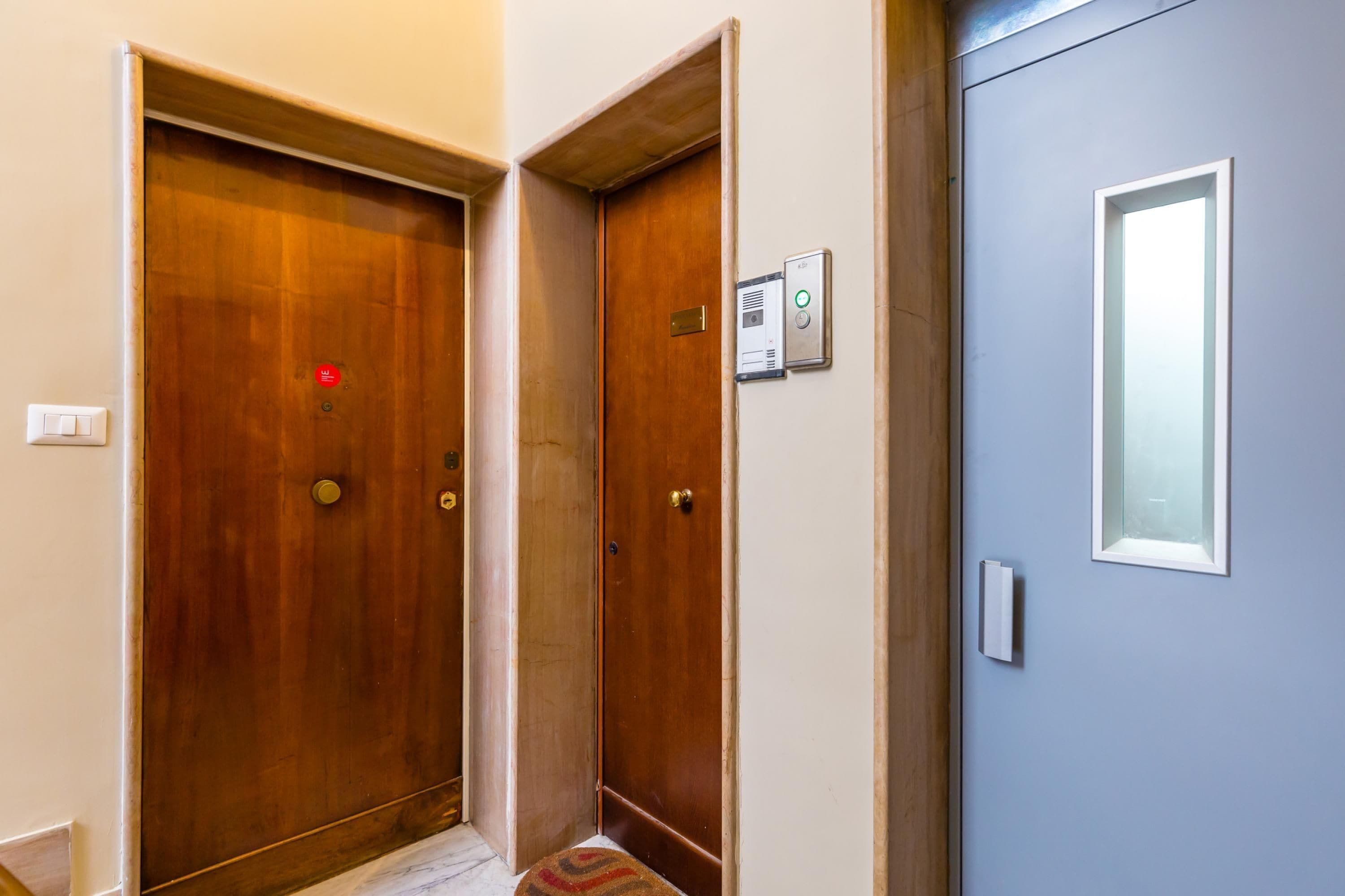 Corredor com duas portas de madeira, uma delas com um toque e um interruptor de luz, e uma porta azul com janela.