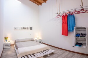 Quarto com cama, mesas de cabeceira, prateleira na parede com roupas e um cabideiro em formato de coração.
