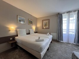 Quarto de hotel com duas camas, obras de arte nas paredes, uma janela com cortinas e uma mesa de cabeceira com luminária.