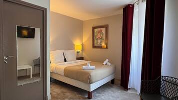 Quarto de hotel com cama, mesa de cabeceira, cadeira, televisão, luminária e um quadro na parede.