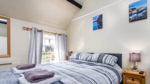 Quarto com uma cama, duas mesas de cabeceira, um criado-mudo, uma janela com cortinas e duas quadros pendurados na parede.