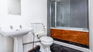 Casa de banho com lavatório suspenso, sanita e cabine de duche com parede de vidro.