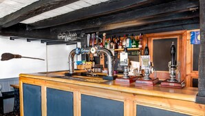 Uma área de bar com balcão de madeira, diversas torneiras e uma vassoura pendurada na parede.