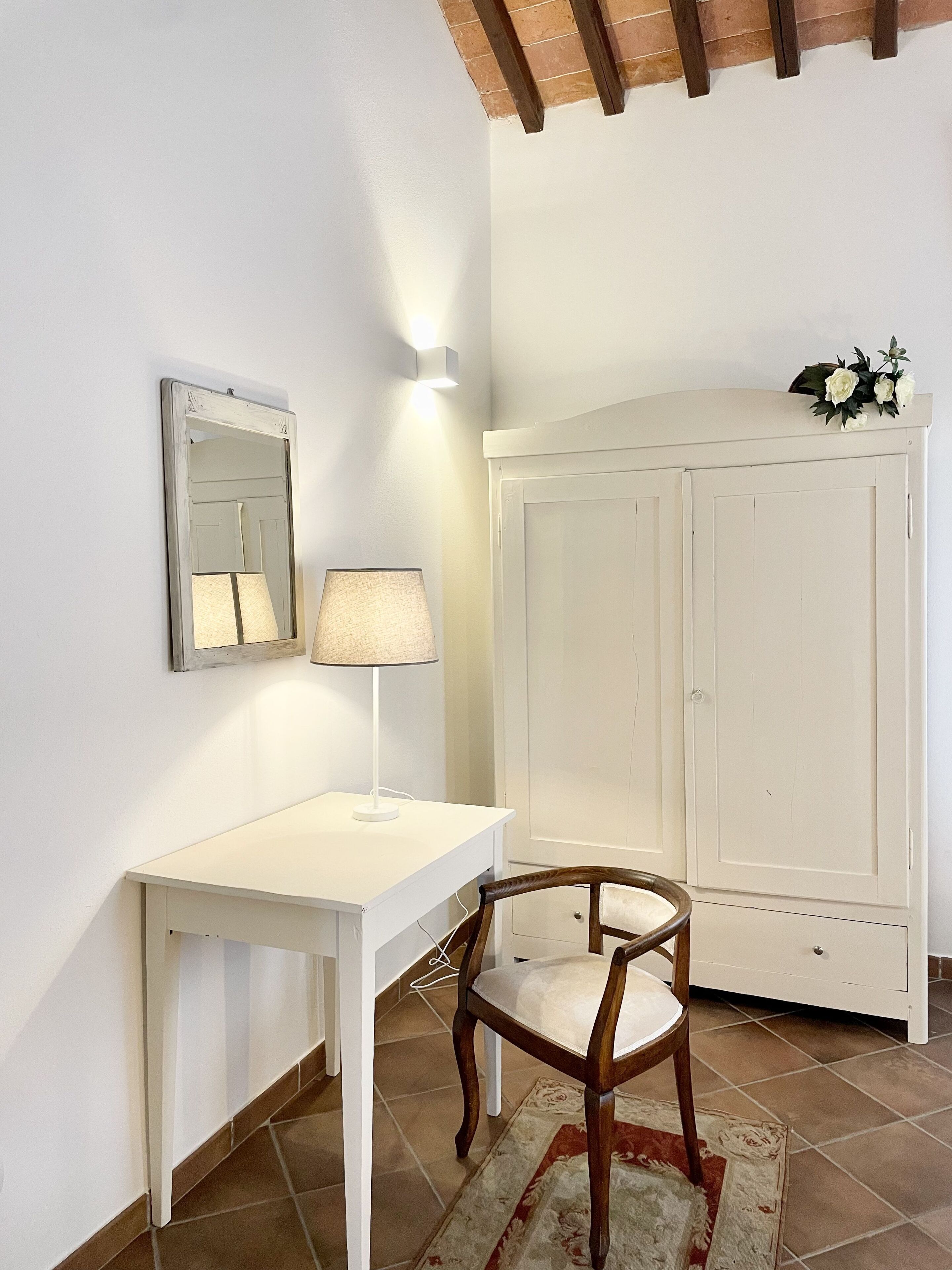 Quarto com escrivaninha branca, cadeira, espelho, abajur e guarda-roupa.