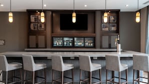Uma área de bar com um balcão comprido, vários bancos e uma televisão acima.