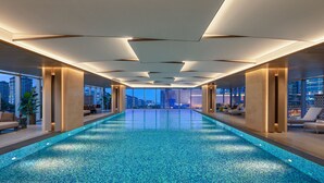 Piscina interior moderna com vista para a cidade, apresentando um design alongado e um chão revestido de azulejos.