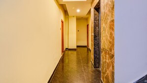 Um corredor com parede de mármore, luminária no teto e uma porta no final.