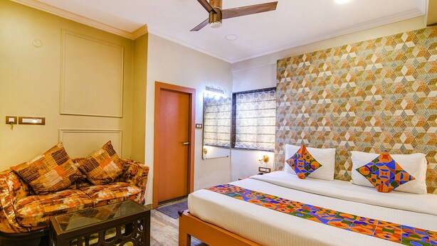 Quarto com cama, sofá, ventoinha no teto e janela com cortinas.