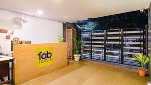 Uma área de recepção com uma mesa de madeira, uma placa com a inscrição "fab hotels" e vista para uma varanda com guarda-corpo.