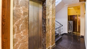 Um elevador com paredes de mármore, uma escadaria com grades de metal e um teto com claraboia.