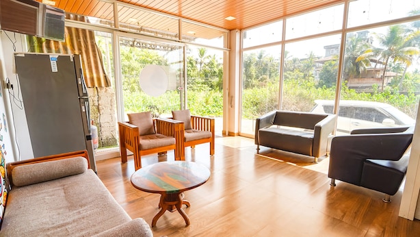 Quarto espaçoso com piso de madeira, uma janela ampla com vista para o verde, um refrigerador e dois sofás.